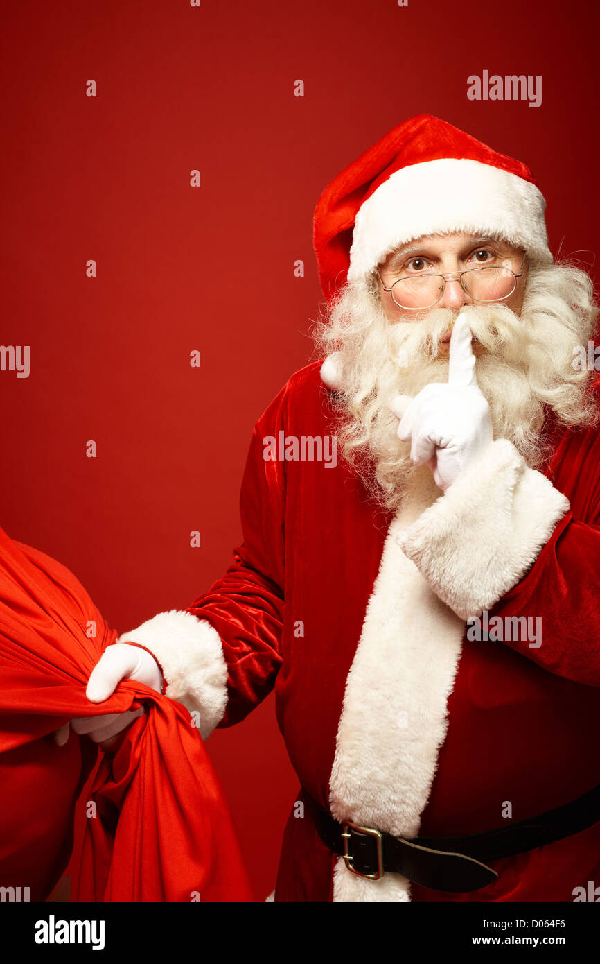 Portrait of Santa Claus with huge red sack keeping forefinger by his ...