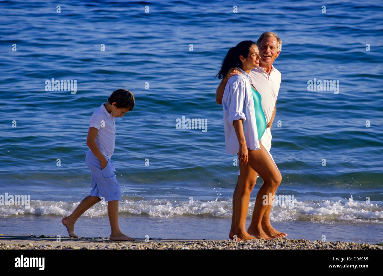 Sulky boy walking behind couple with pregnant woman on seashore Stock ...