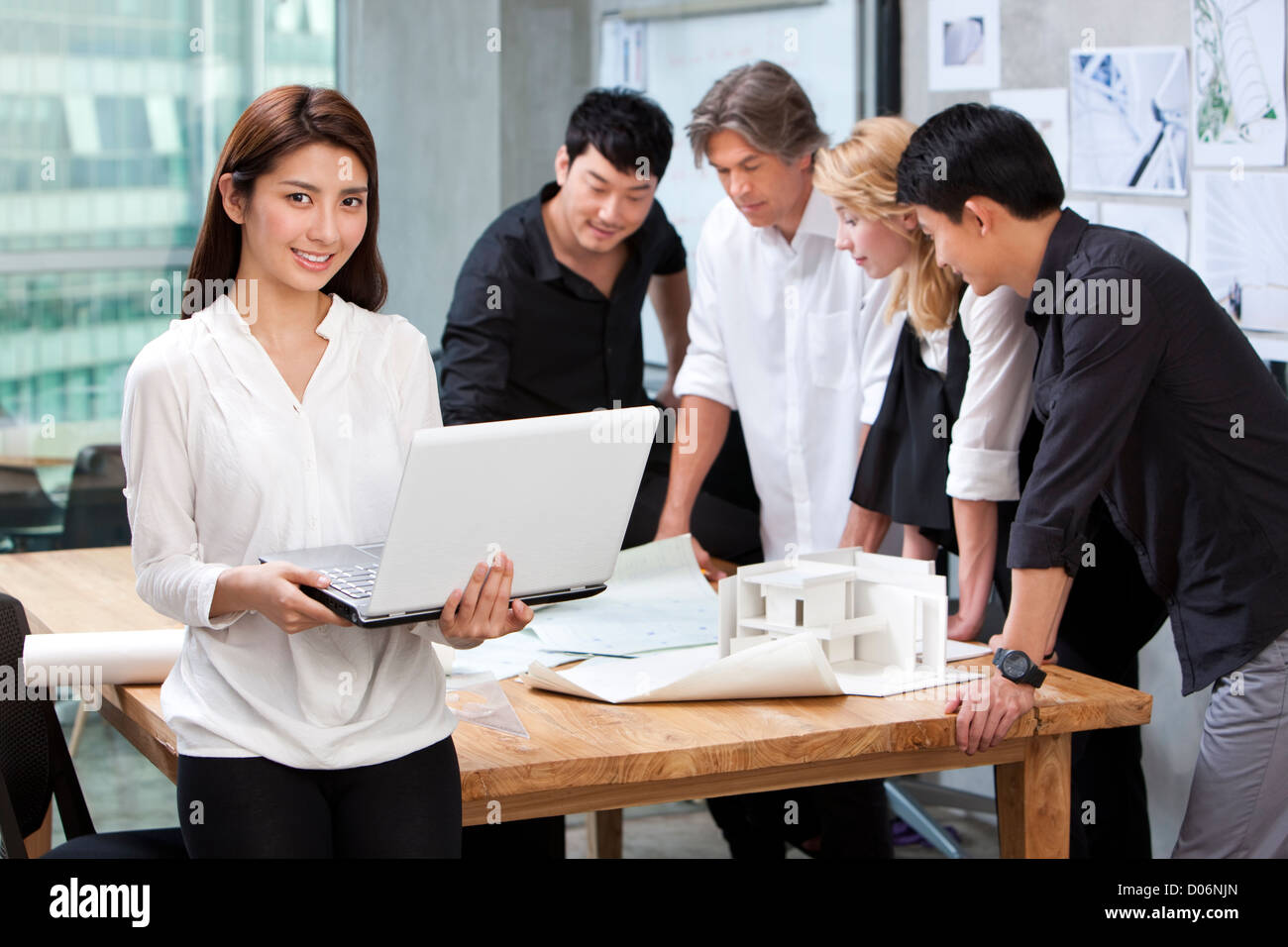 Architect holding laptop in studio with her team in background Stock ...