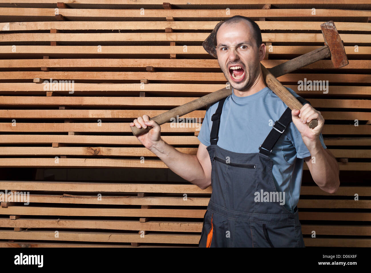 Angry worker with axe and hammer. Horizontal shot with wood in the ...