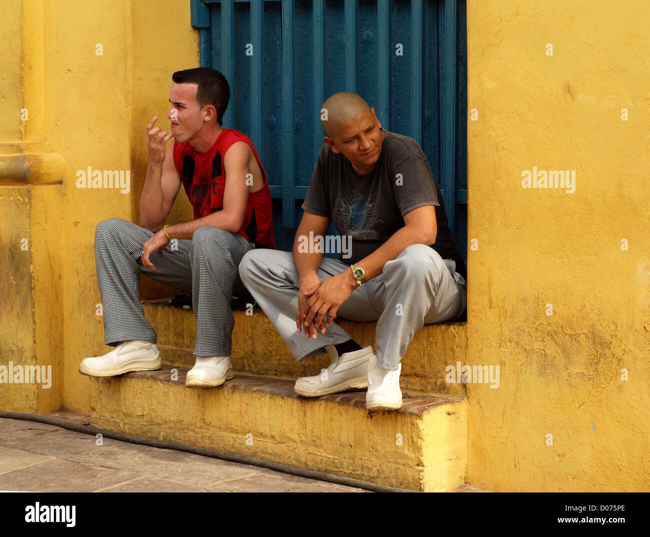 two young Cuban males pass the time on a colourful step on the street ...