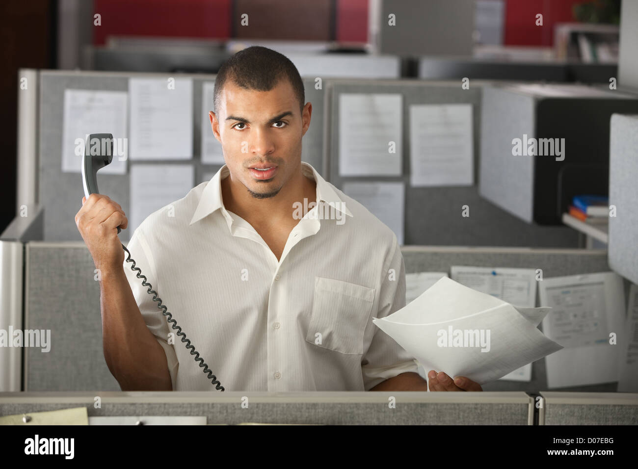 Frustrated office worker with papers holds a phone away from his ear ...