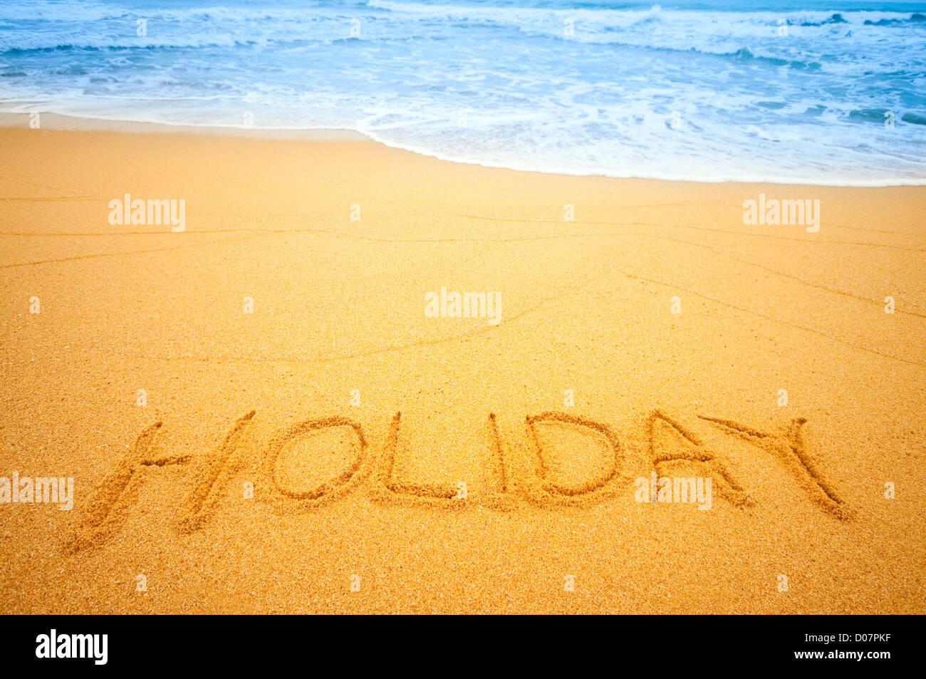Holiday written in the sand on the beach blue waves in the background ...