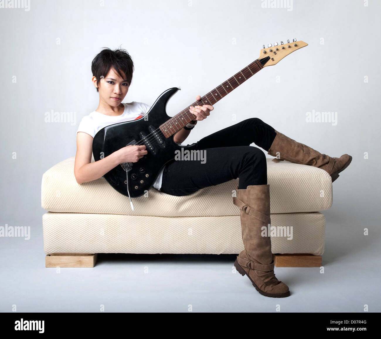 Punk Rockstar holding a guitar sitting on sofa Stock Photo - Alamy
