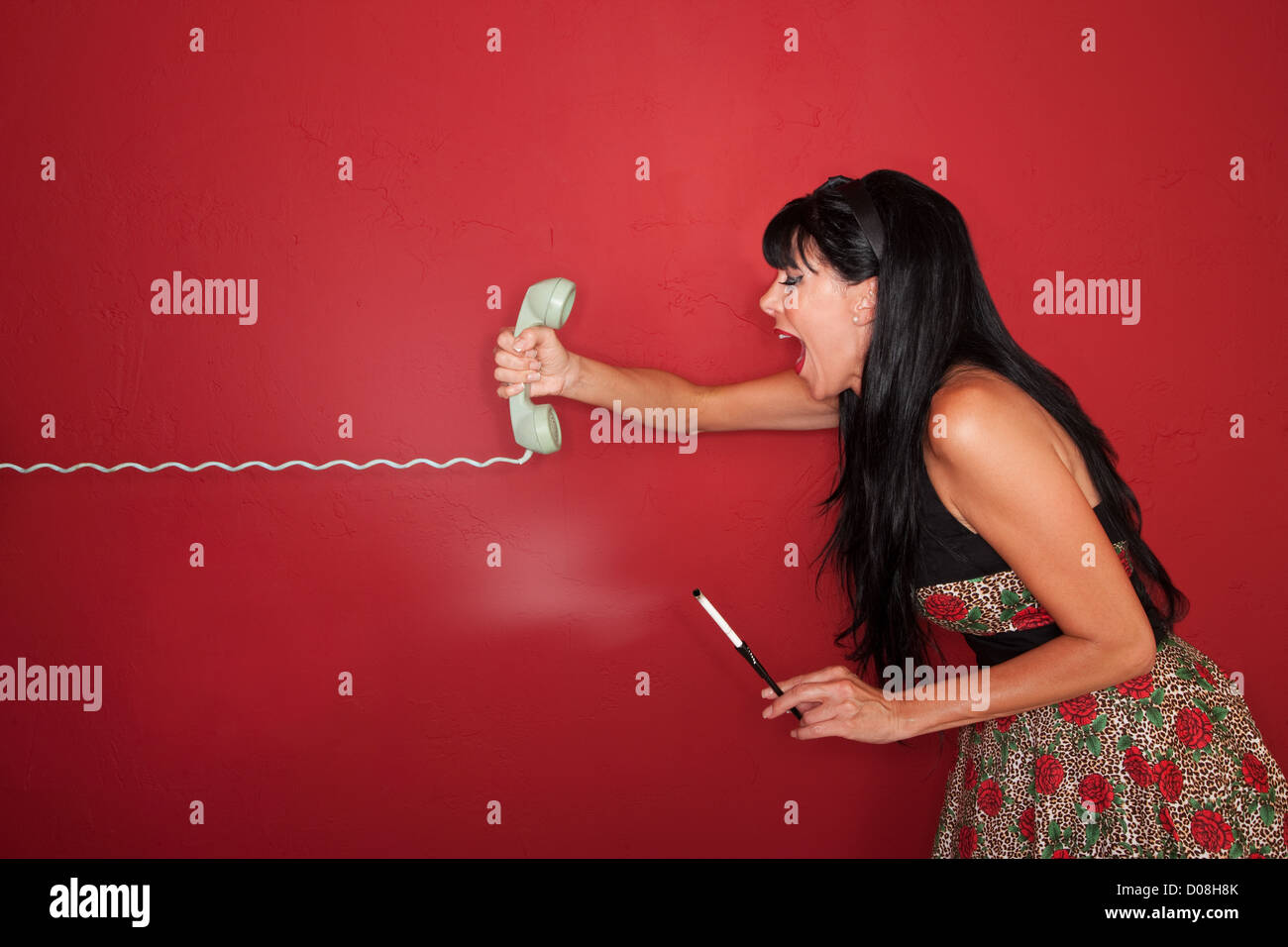 Frustrated Caucasian woman yells on phone call over maroon background ...