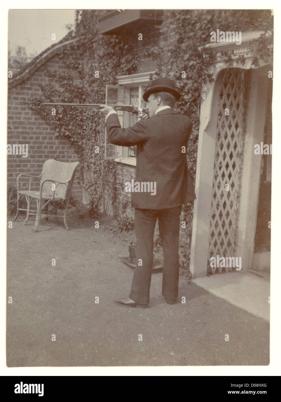 Edwardian man outside his house with an air rifle, looking as if he is ...