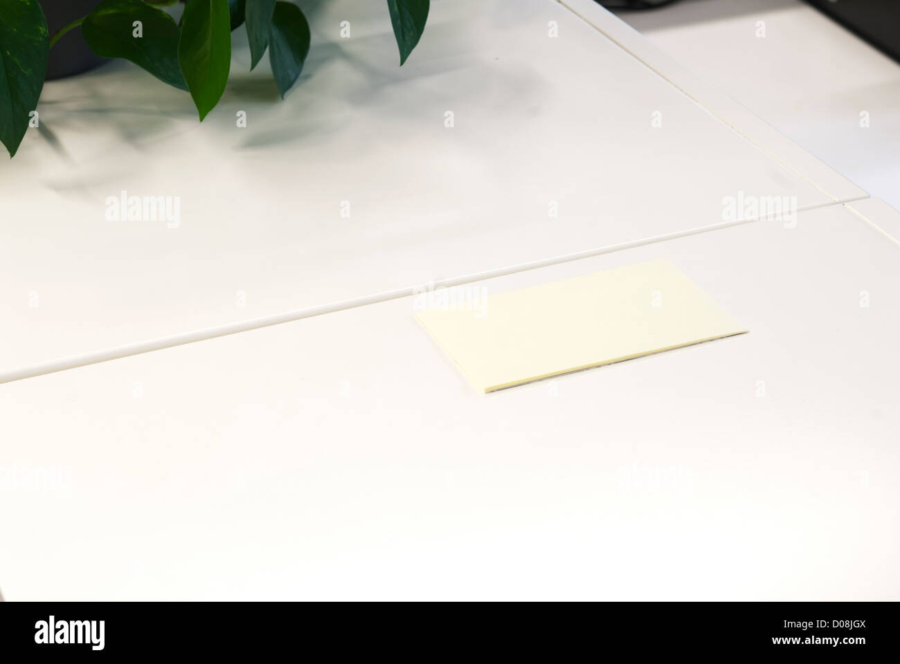 Blank yellow post it note lying on white desk beside a potted plant in ...
