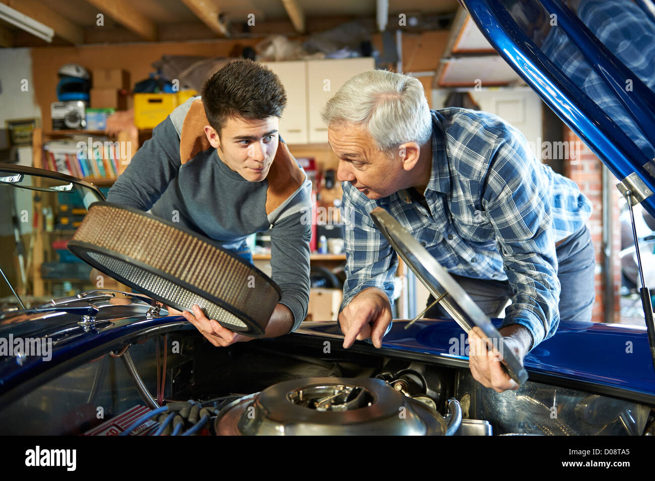 father and teenage son working together in the garage on a classic car ...