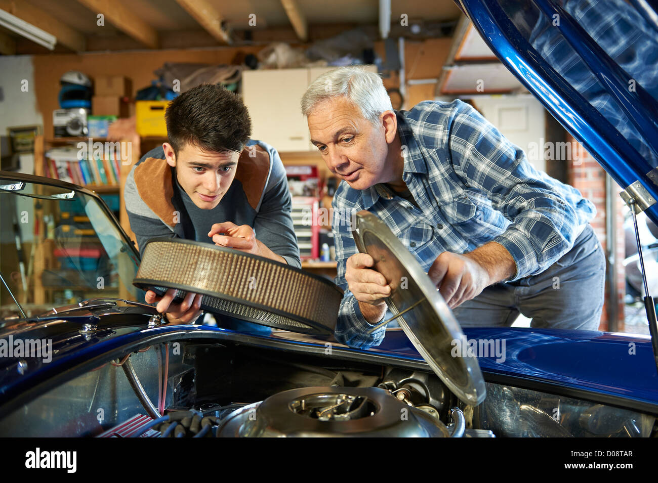 father and teenage son working together in the garage on a classic car ...