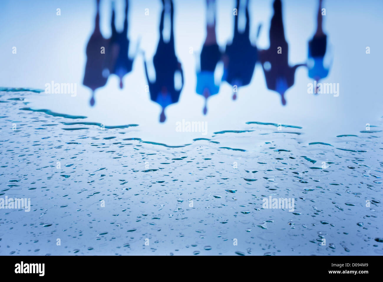 Group of people reflecting in the wet glass surface covered with ...