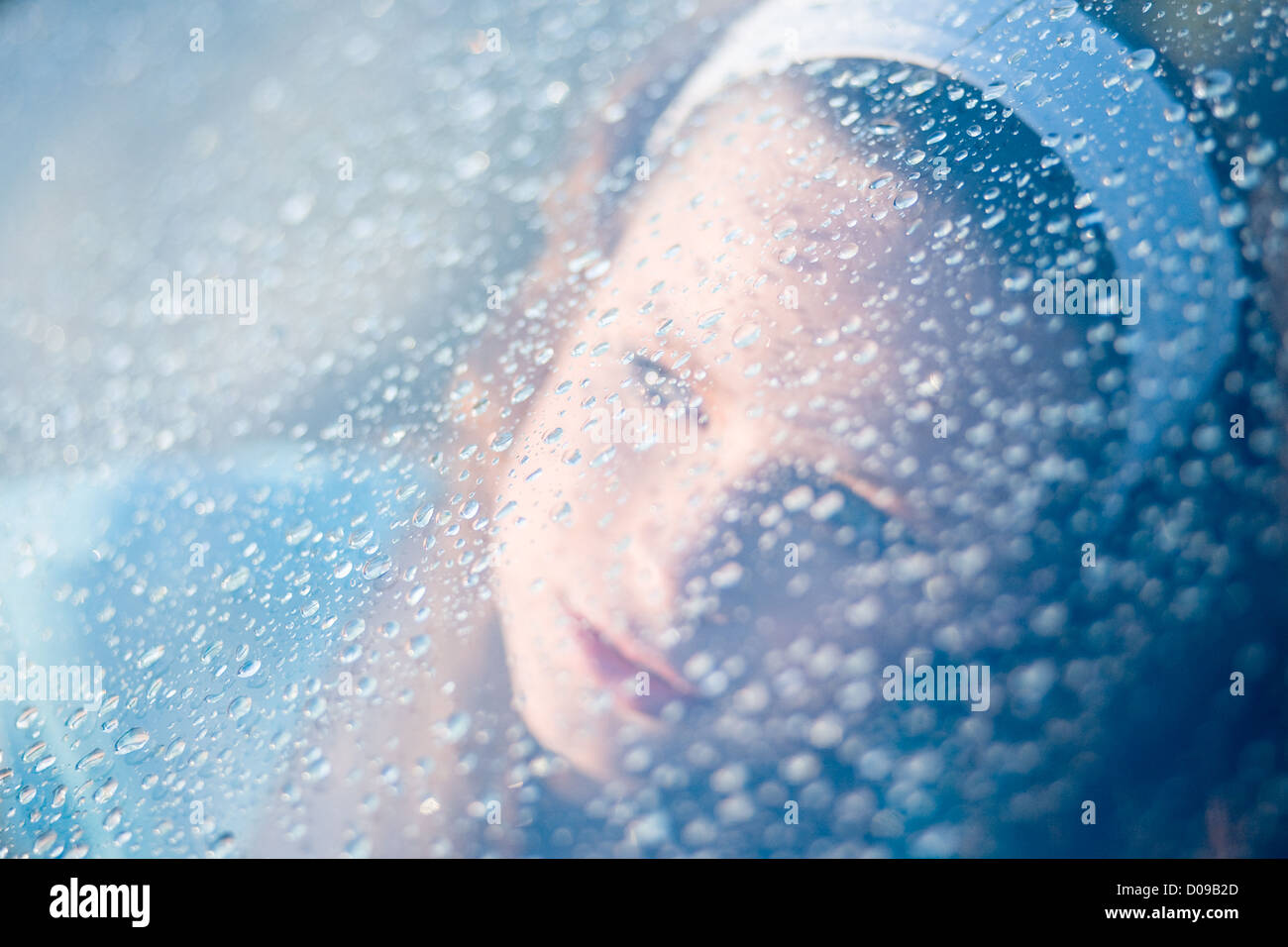 Young girl looking through window after rain Focus on drops Stock Photo ...