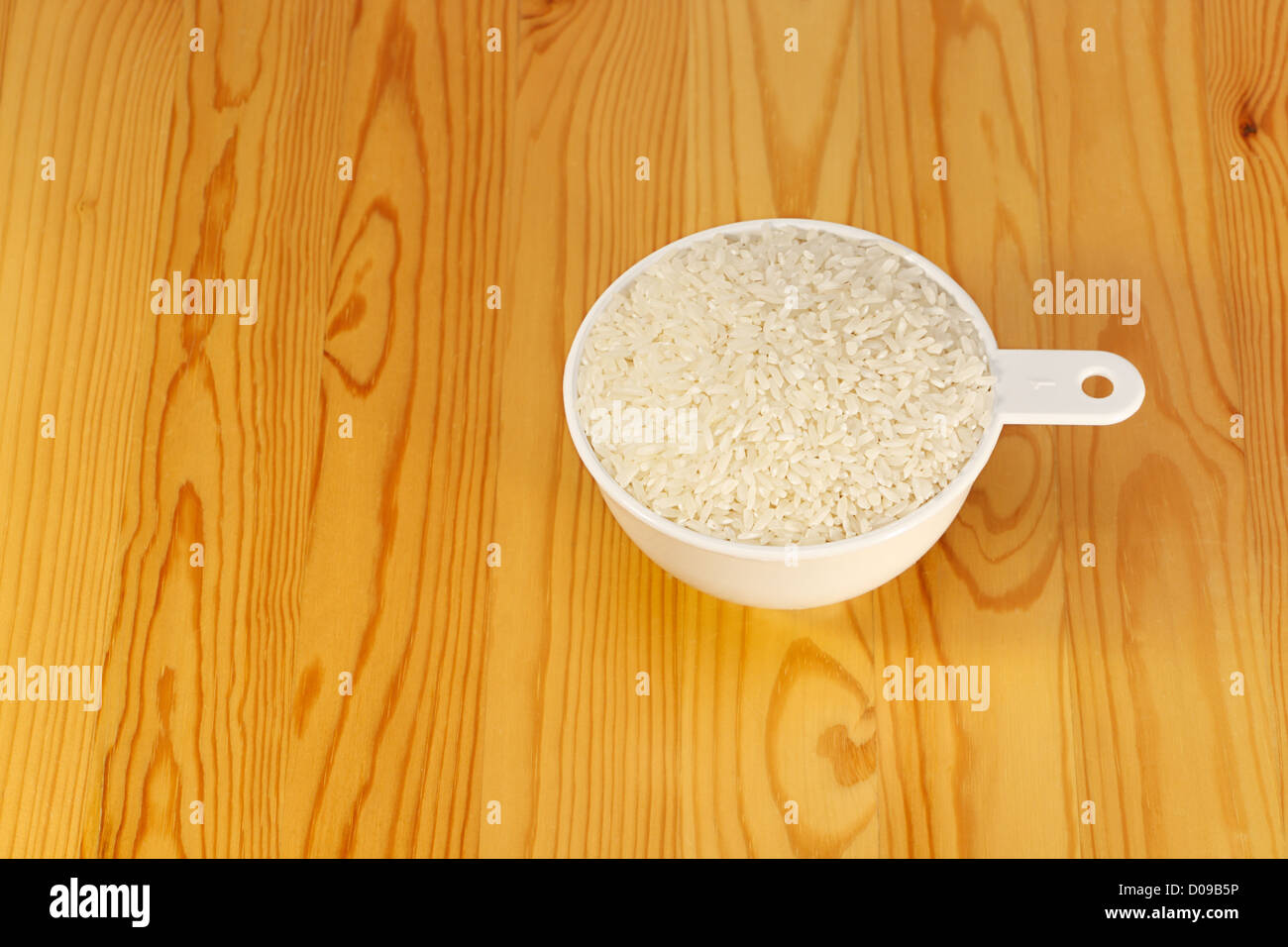 Measuring cup of raw rice on wood kitchen table Stock Photo - Alamy
