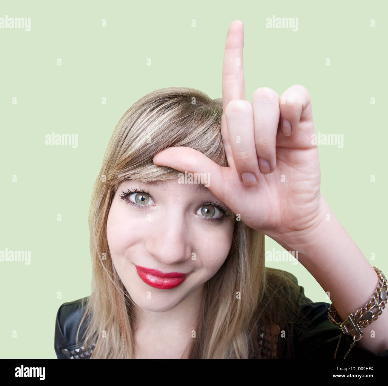 Cute young Caucasian woman makes loser sign on her forehead over green ... Cute young Caucasian woman makes loser sign on her forehead over green ...
