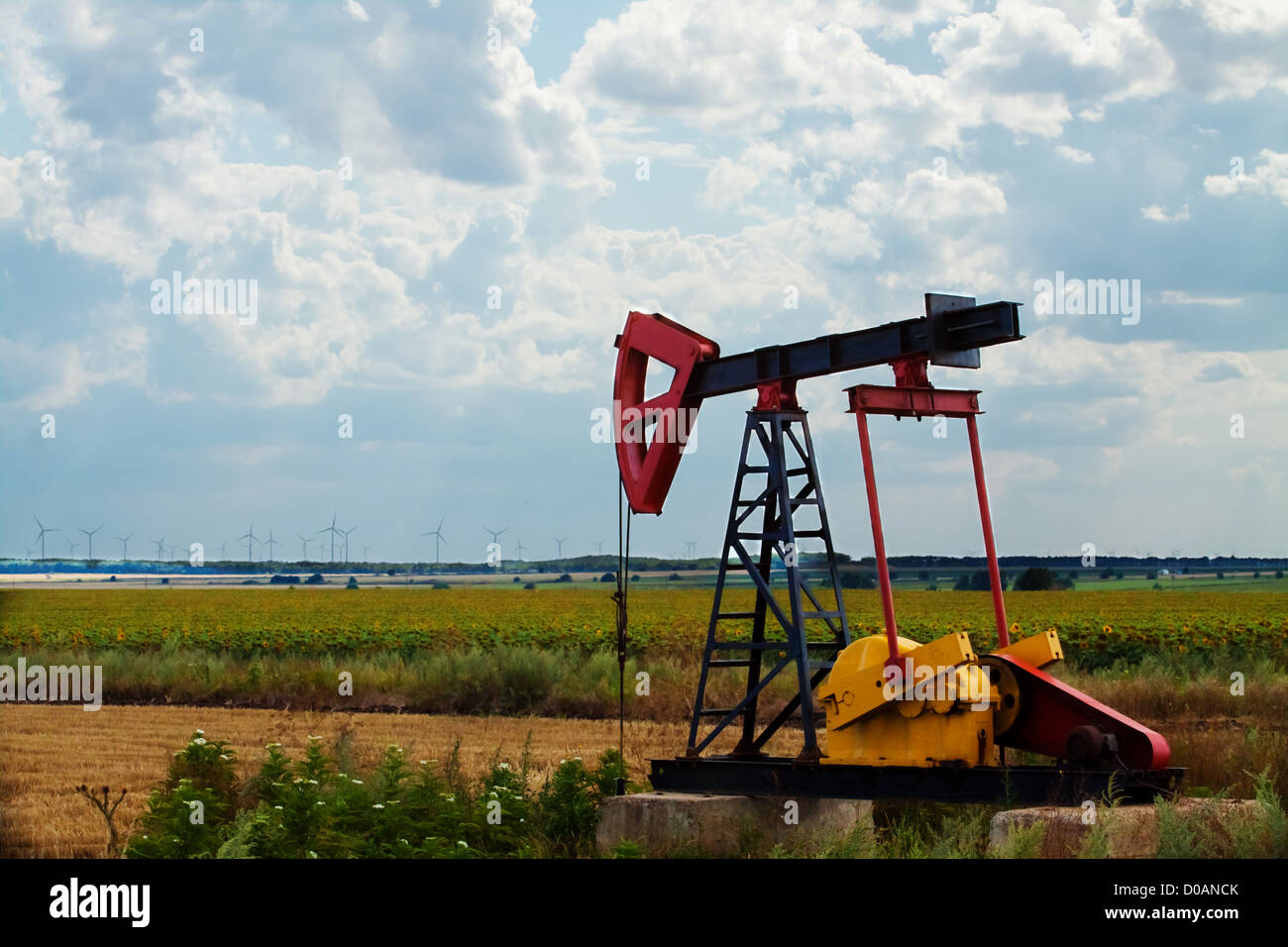 Old oil rig with sunflower field and modern wind generators, horizontal ...