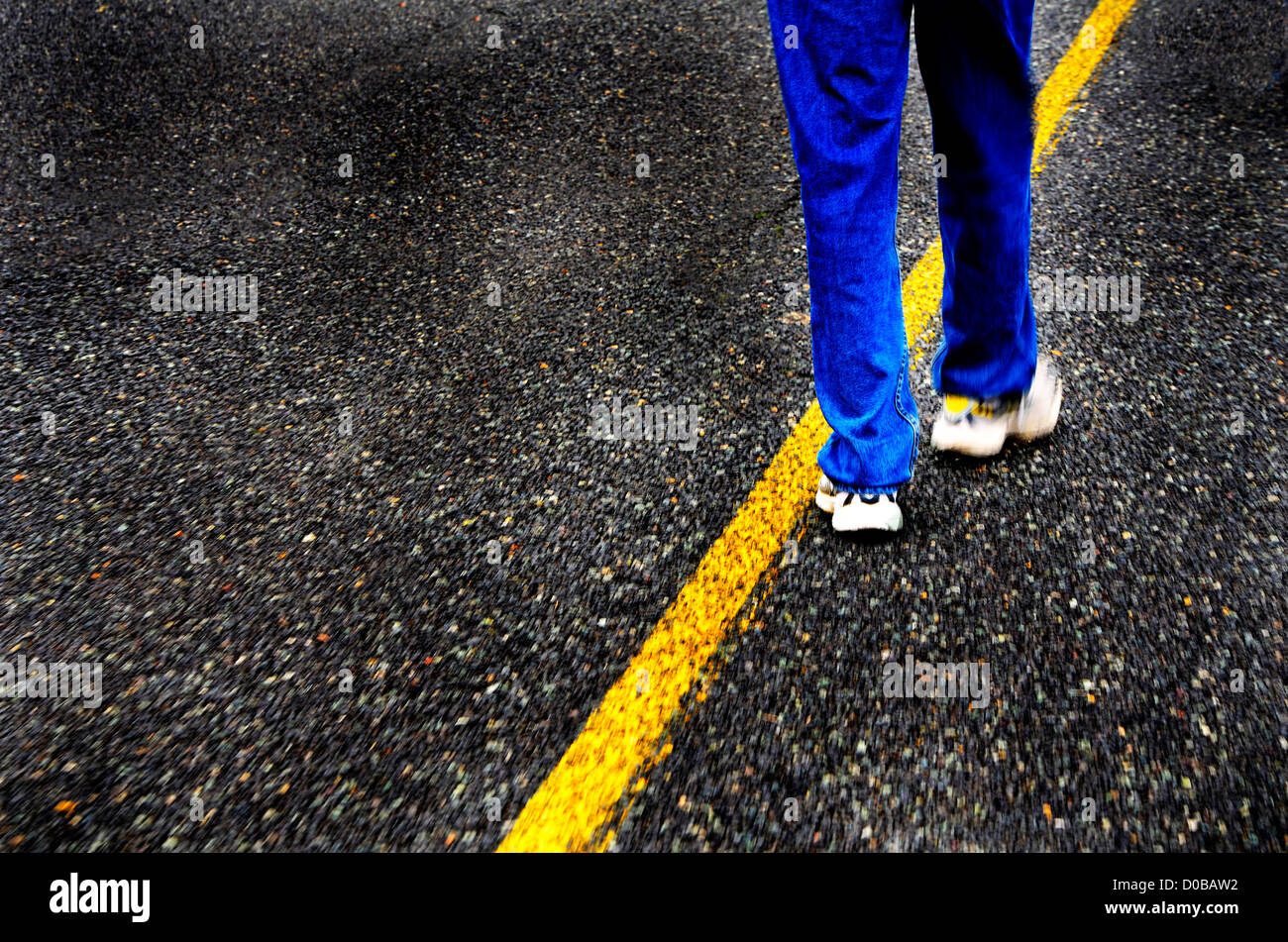Person wearing blue jeans walking down yellow line of road Stock Photo ...
