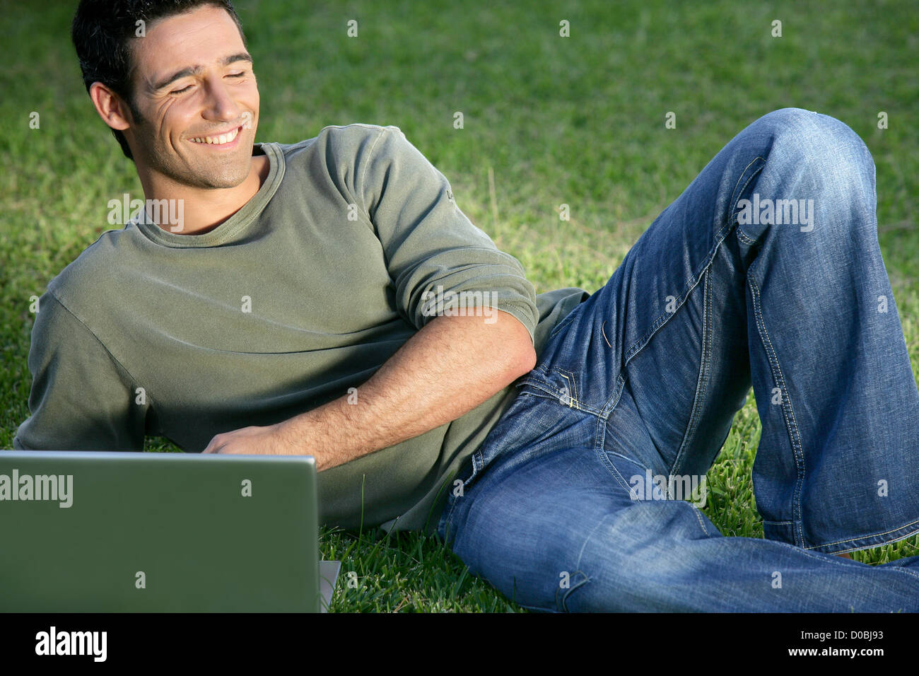 Happy man sat in field with laptop Stock Photo - Alamy