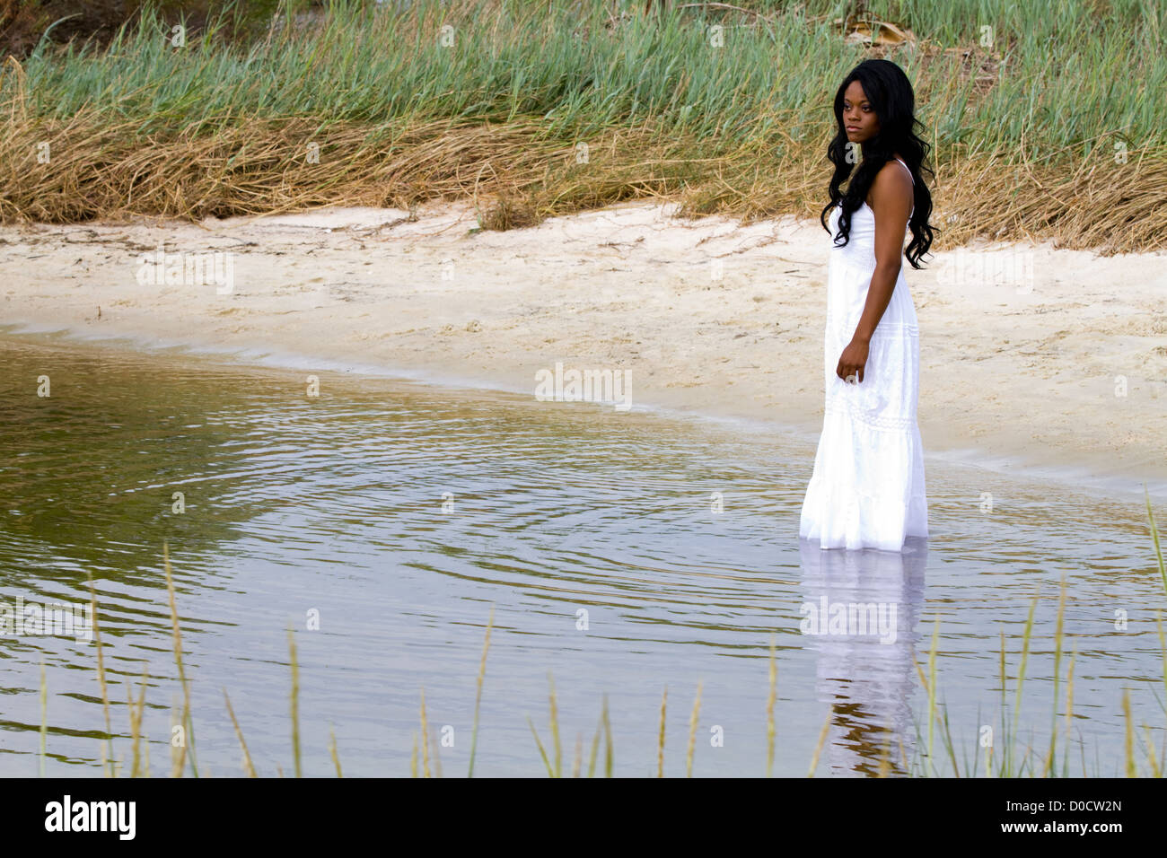 Lonely African American woman stands downcast in shallow water with a ...
