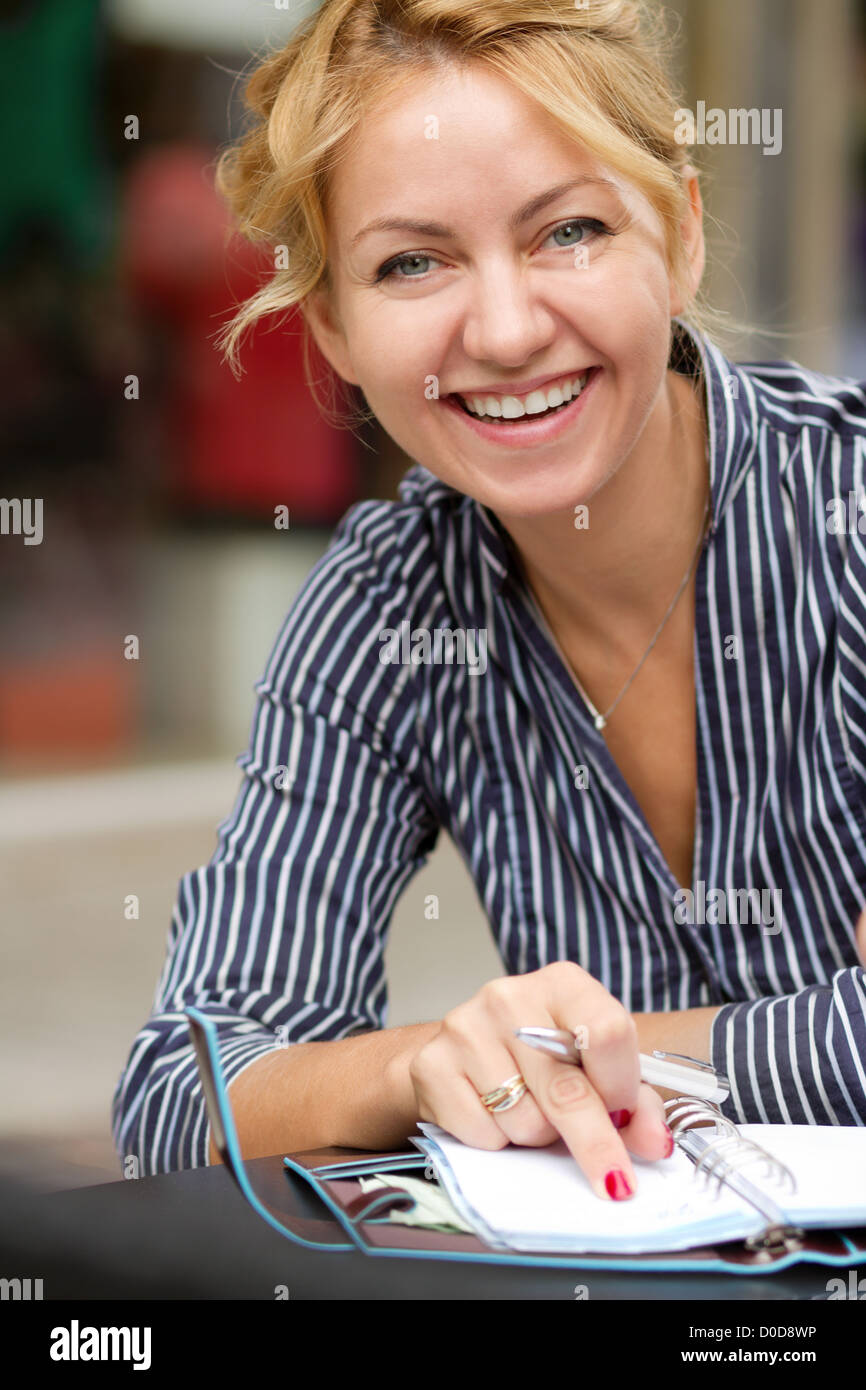 Attractive blond businesswoman writing in her diary at business lunch ...