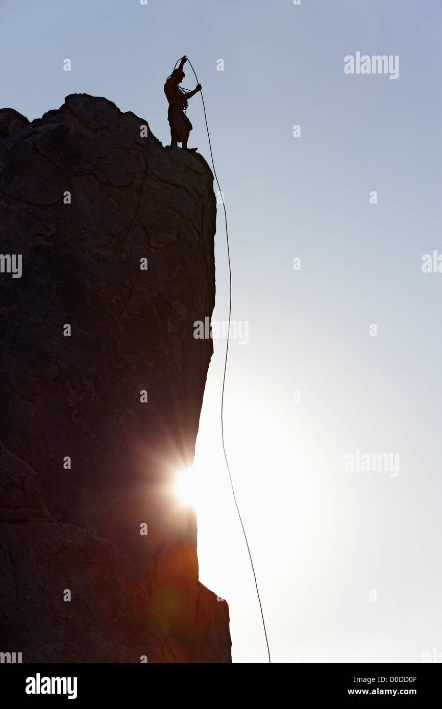A climber prepares rappel down overhanging cliff face adjusting his ...