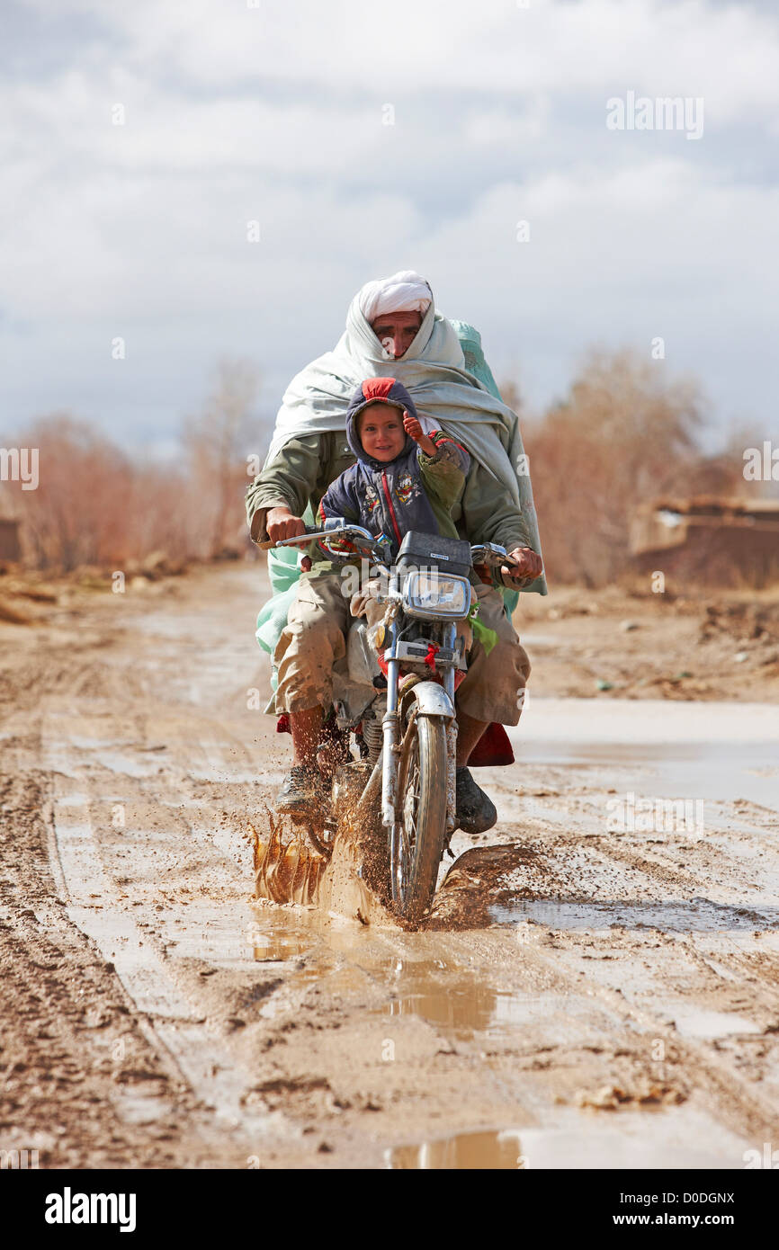 Afghan man rides motorcycle on muddy road his veiled wife young son who ...