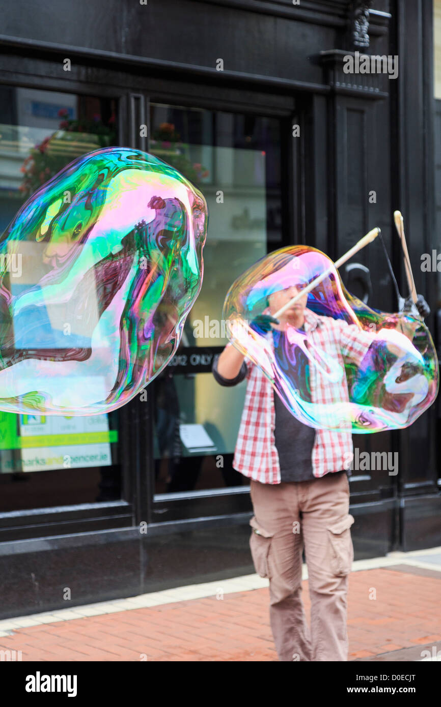 Irish street entertainer making 2 large bubbles with two sticks in city ...