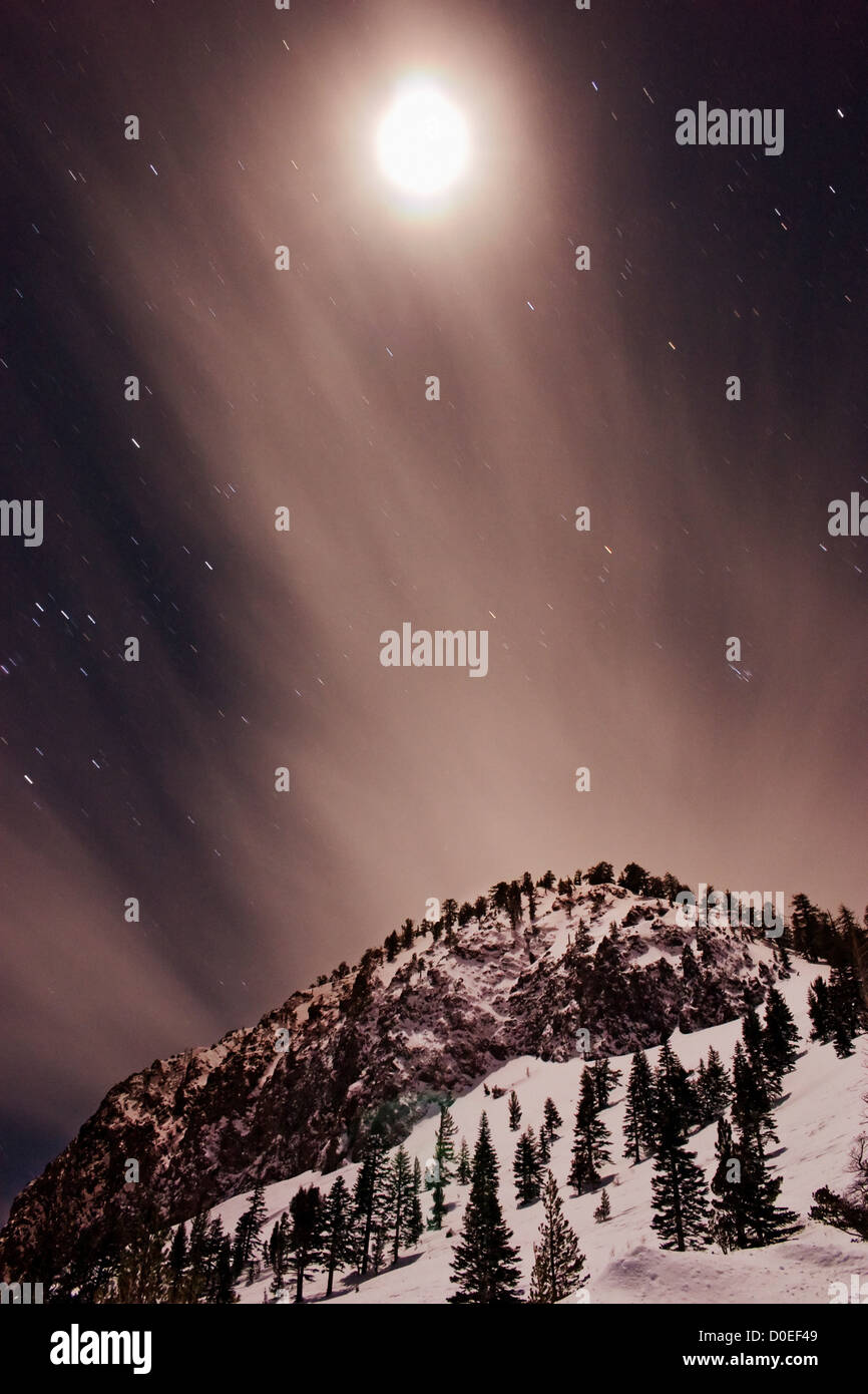 The moon rises while clouds rush through its brightening light in a ...