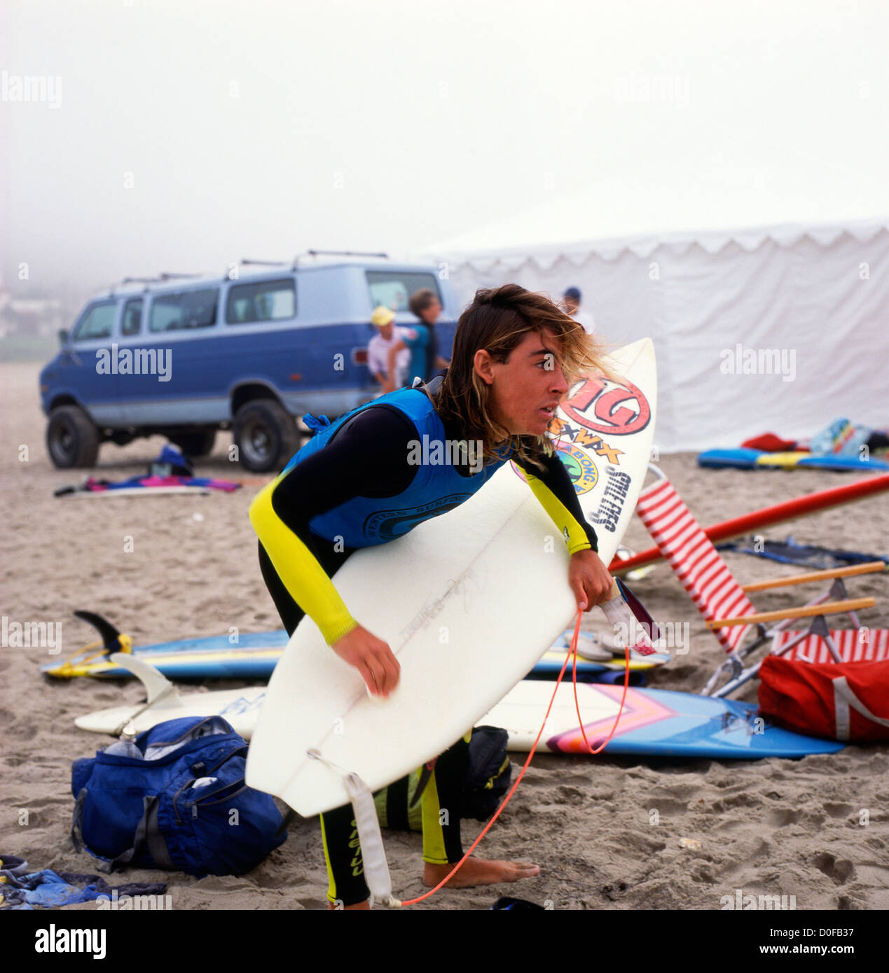 Young man surfer looking at waves waxing surfboard during surfing ...