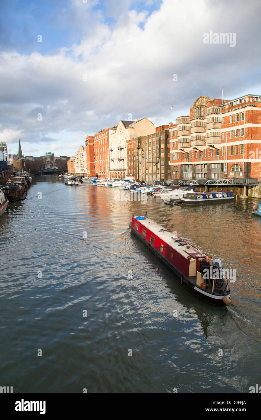 A red narrow boat makes its way along the floating harbour in Bristol ...