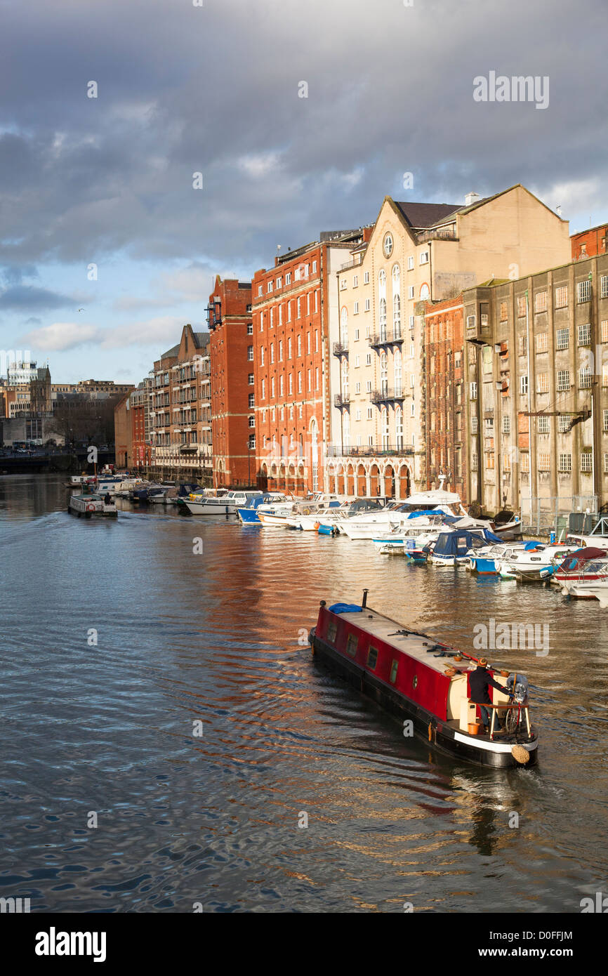 A red narrow boat makes its way along the floating harbour in Bristol ...