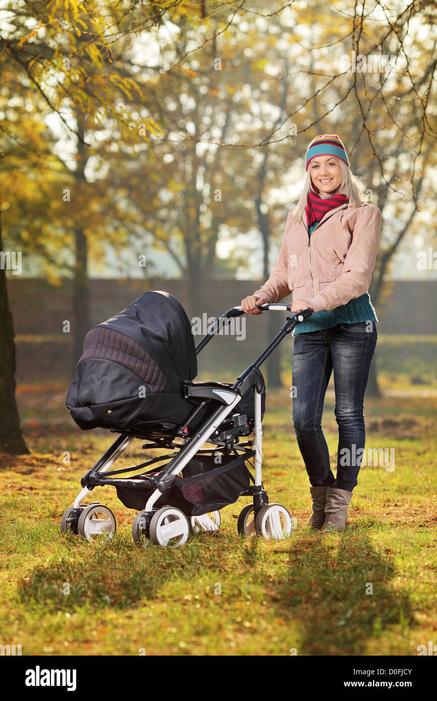 A smiling mother posing with a baby stroller in a park in autumn Stock ...