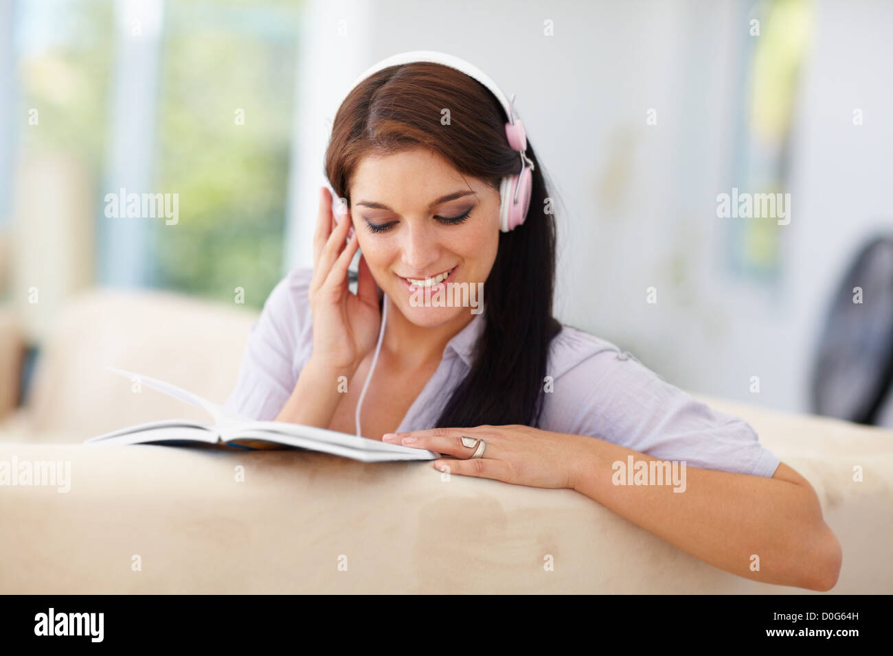 An attractive young woman reading a book and listening to her ...