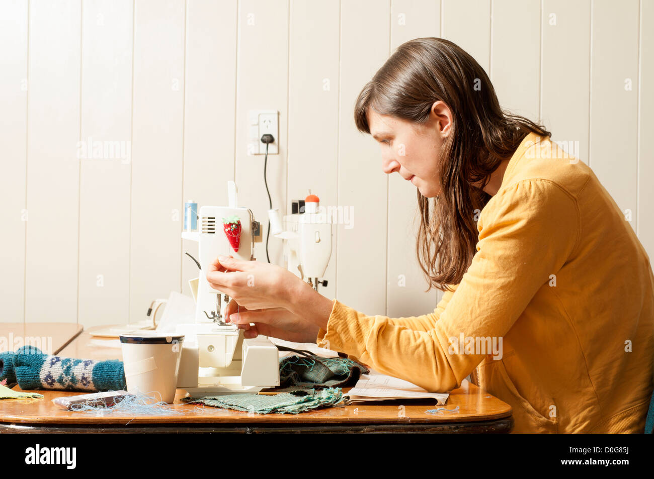 Women sitting at table threading thread into sewing machine with cup of ...