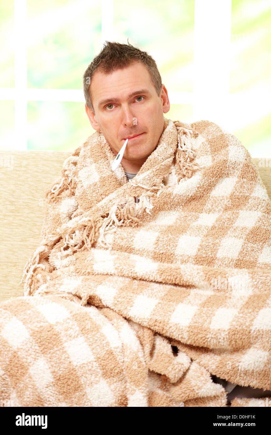 Man with cold sitting on sofa with thermometer in mouth Stock Photo - Alamy
