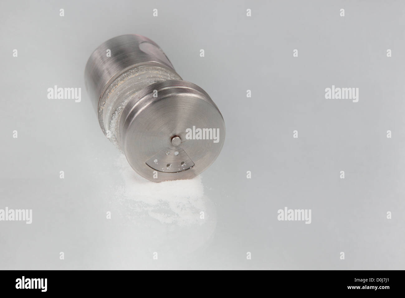 a salt shaker spilled on a white surface. The salt cap is ajar and we ...