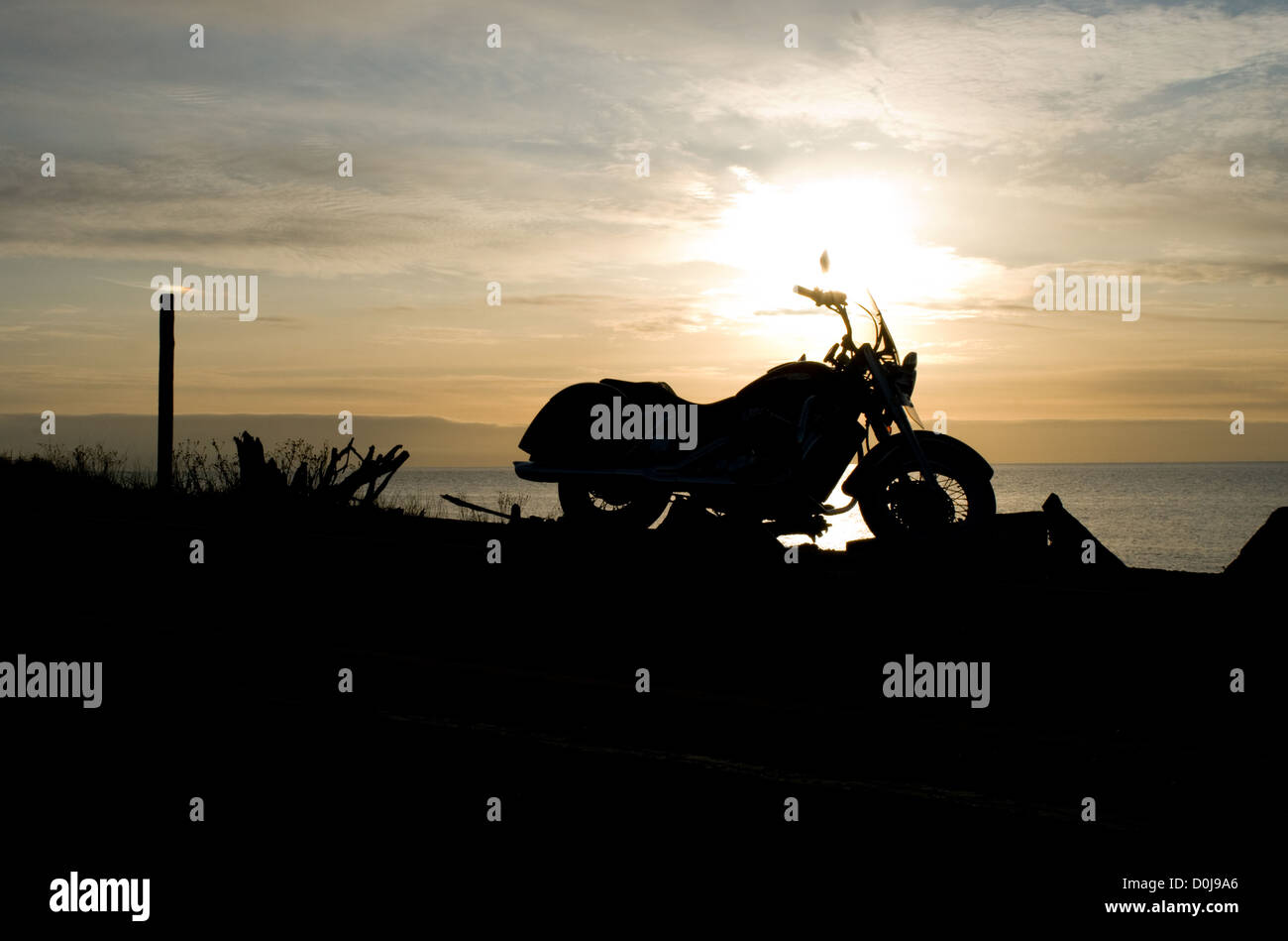 A silhouette of a motorcycle parked on a quiet deserted beach at sunset ...