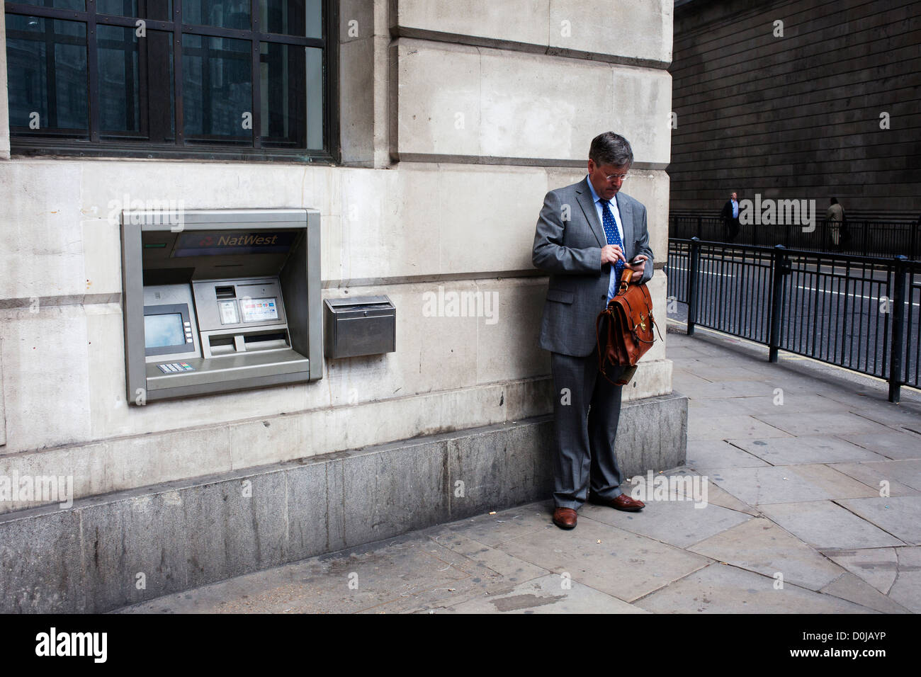 A man standing at a cash machine using his phone Stock Photo - Alamy