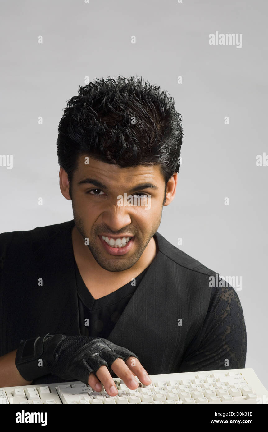 Man typing on a computer keyboard and looking angry Stock Photo - Alamy