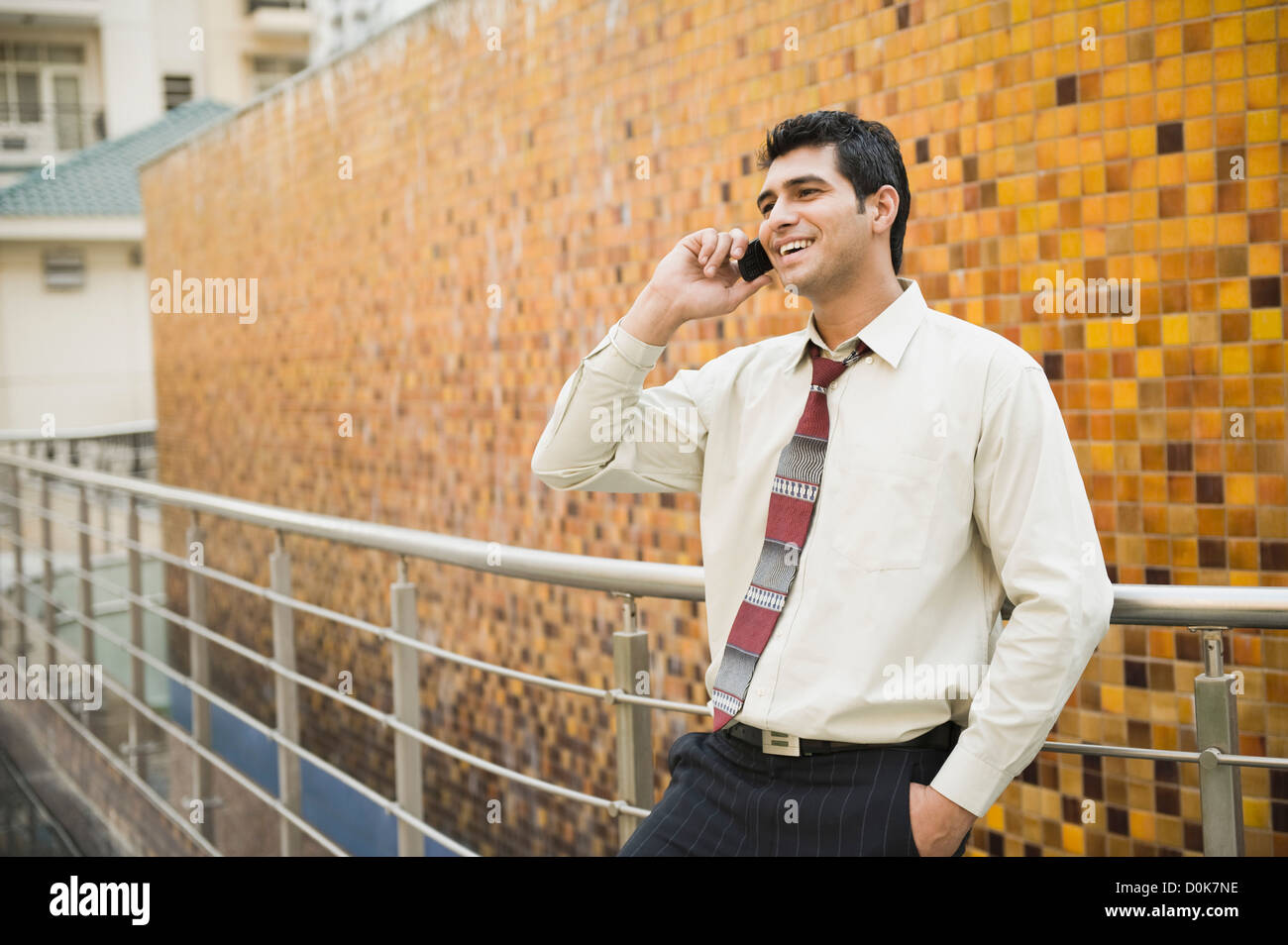 Businessman leaning against a railing and talking on a mobile phone ...