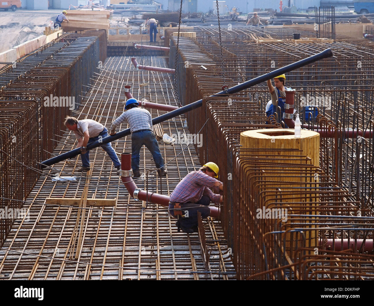 Construction workers handling pipes and working on a metal mesh ...