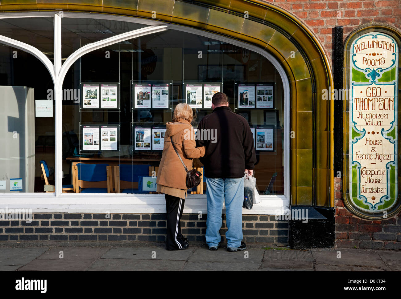 Couple people man and woman looking in estate agent agents shop window ...