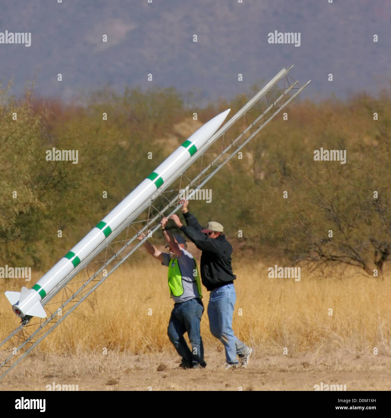 Larry Foster (in dark jacket) lifts long green white rocket on launch ...