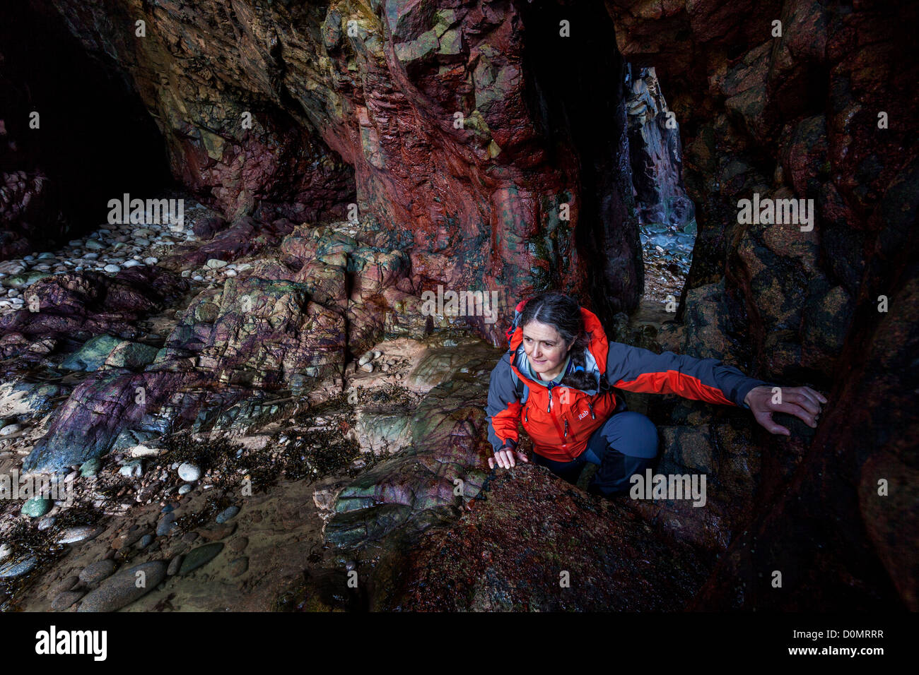 Woman climbing on rocks inside sea cave at Plemont, Jersey, Channel ...