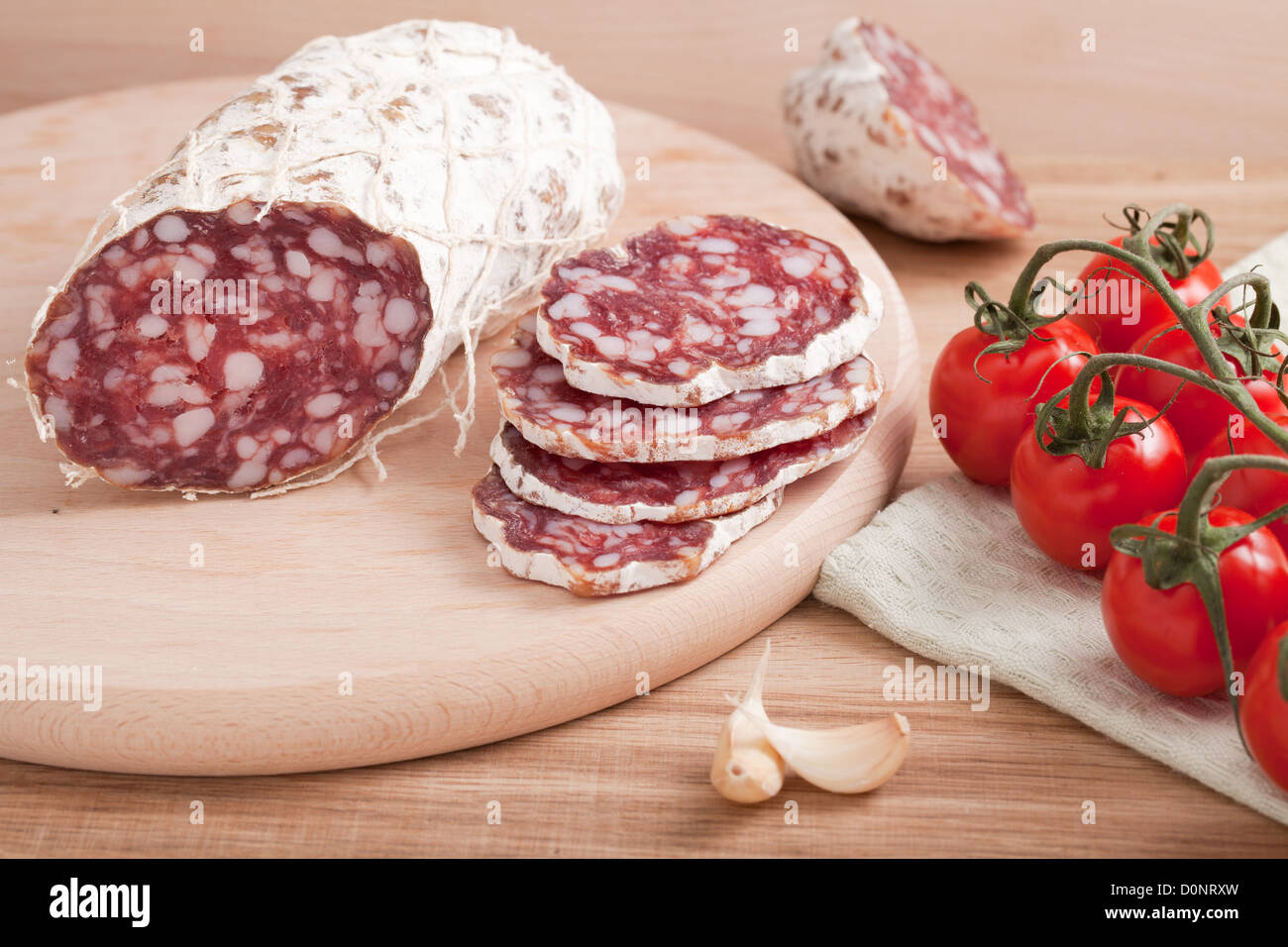 Traditional sliced salami on wooden board with garlic, cherry tomatoes ...
