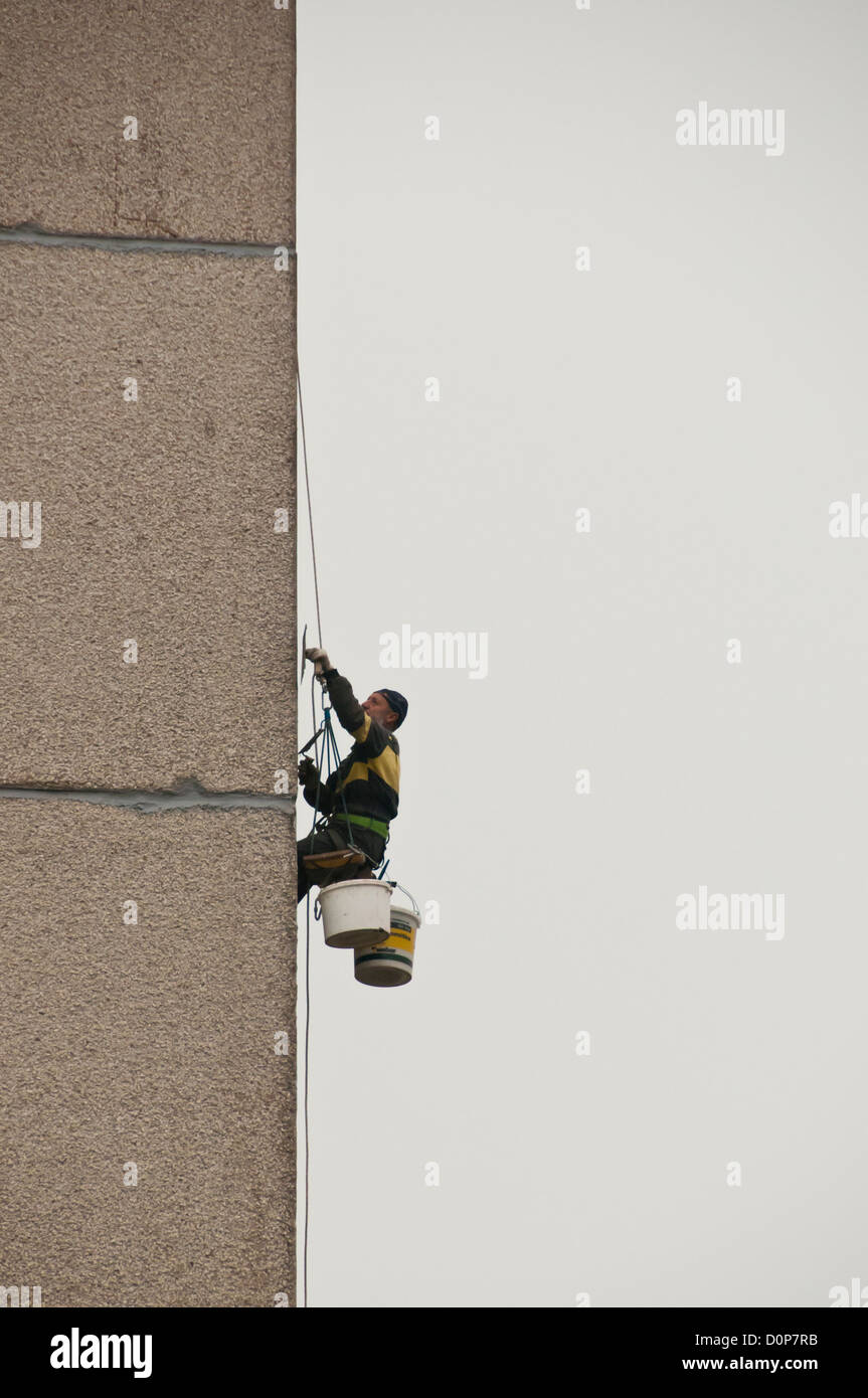 man hanging on ropes and repairing the exterior of a multi-story ...