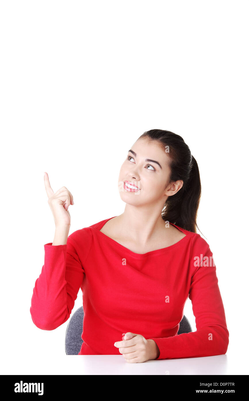 Young woman sitting at the desk and pointing something, isolated on ...