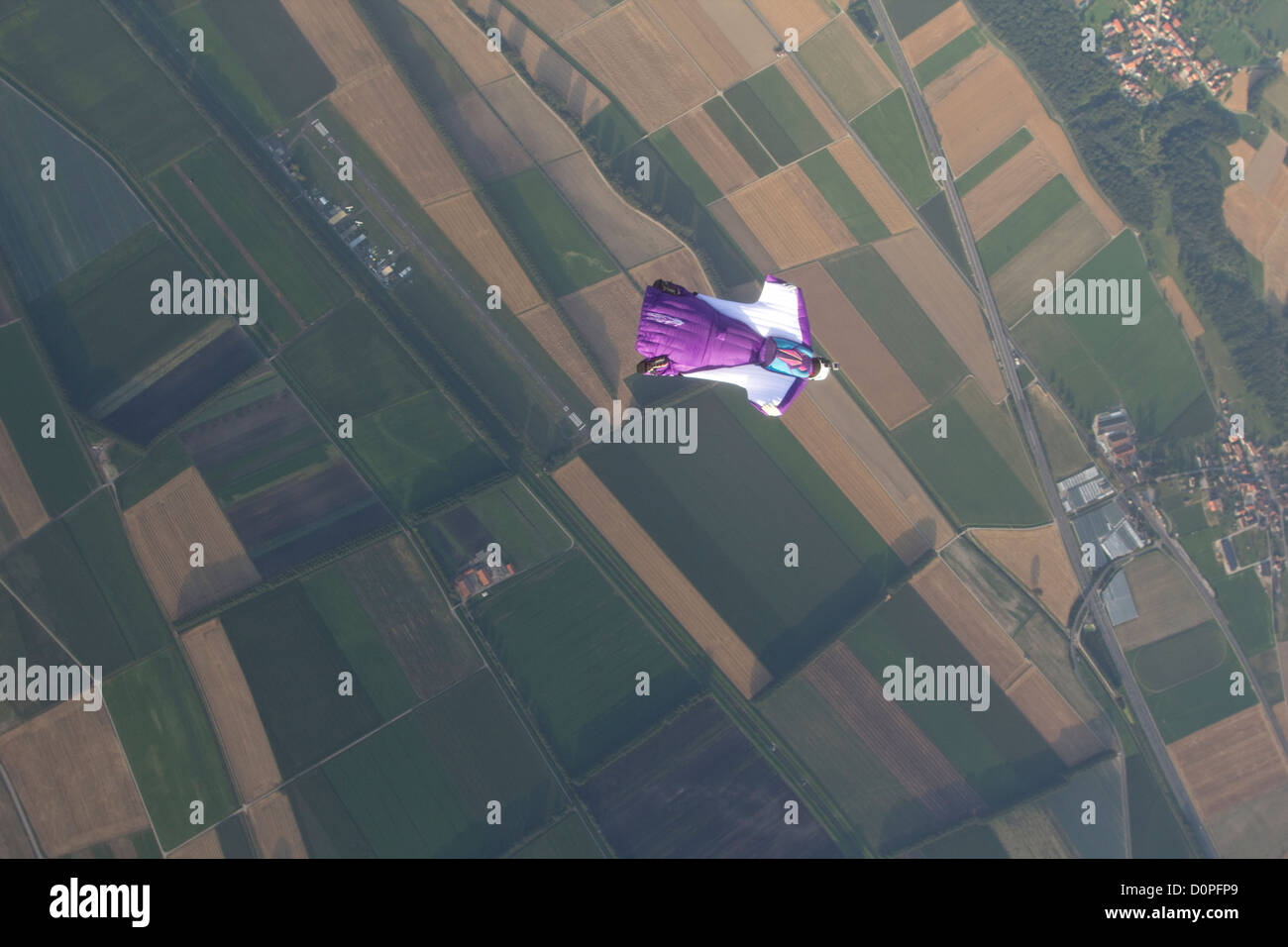 Man with wings is flying free in the sky over green fields. This ...