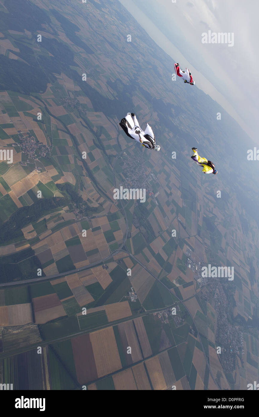 Wingsuit skydivers are flying together in an arrow formation over ...