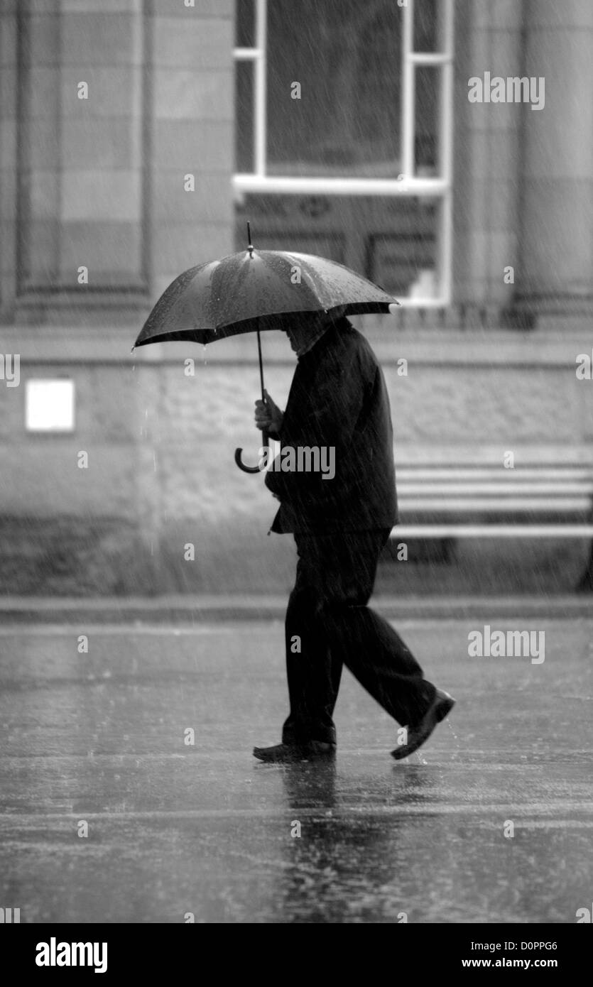 Wimbourn, A man walks across the street in the pouring rain using an ...