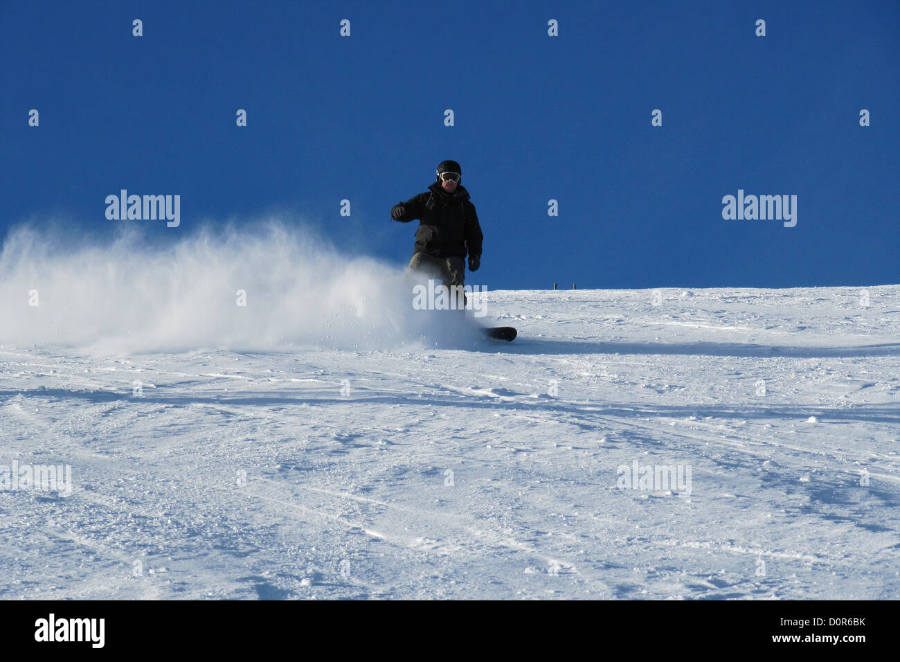 Snowboarder kicking up powder under a blue sky Stock Photo - Alamy
