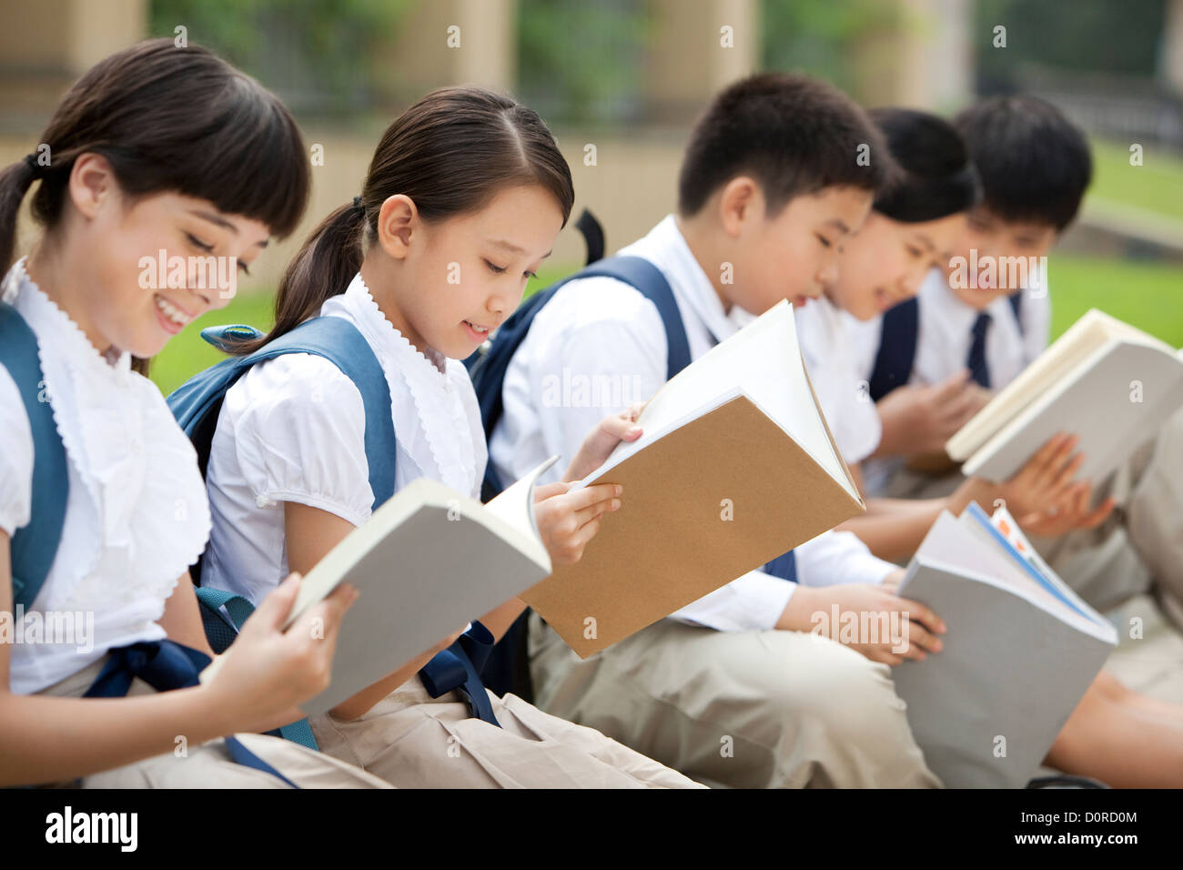 Cute schoolchildren in uniform reading books at school yard Stock Photo ...